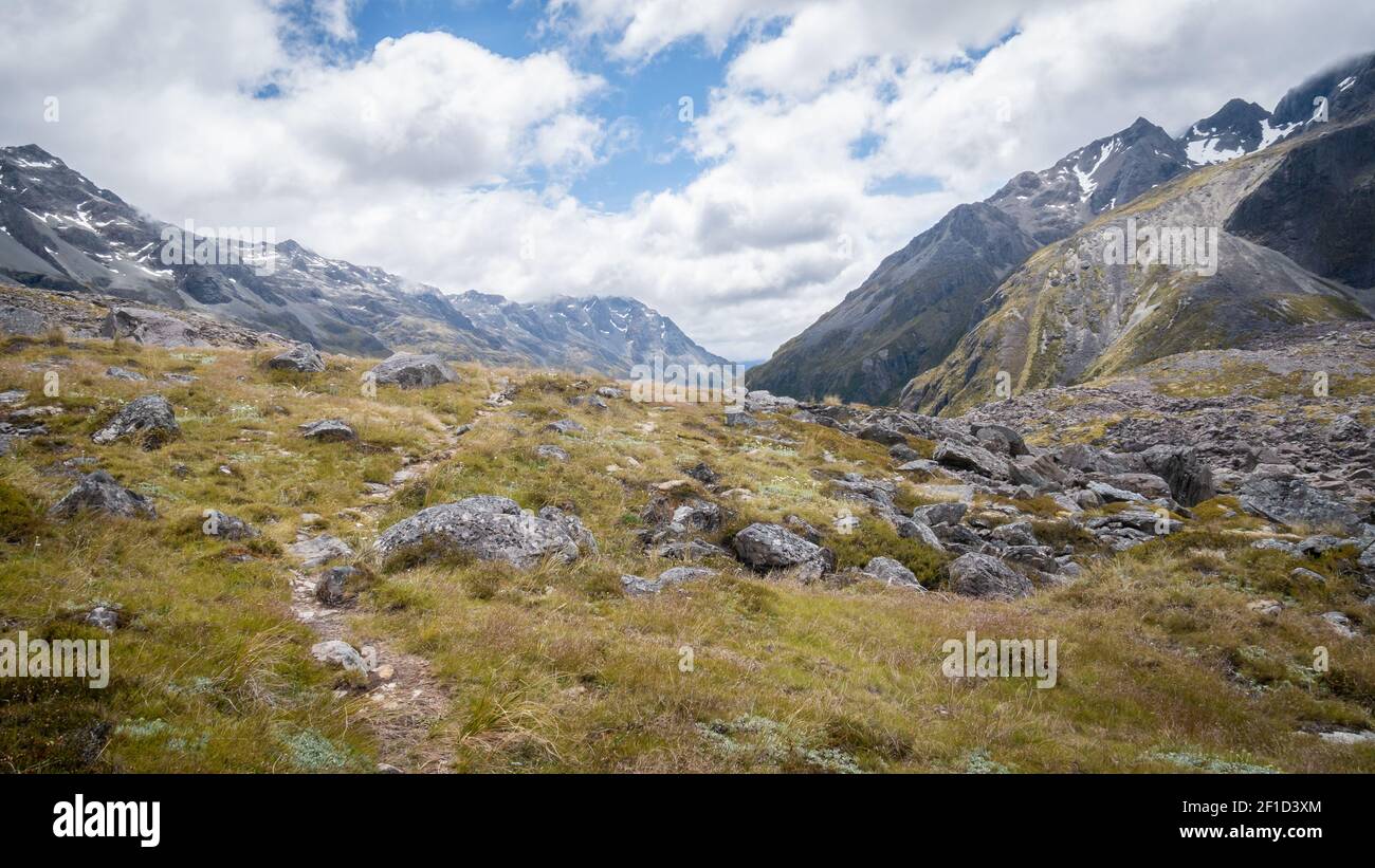 Alpine scenery with mountains, rocks, dry tussocks and cloudy sky, shot ...