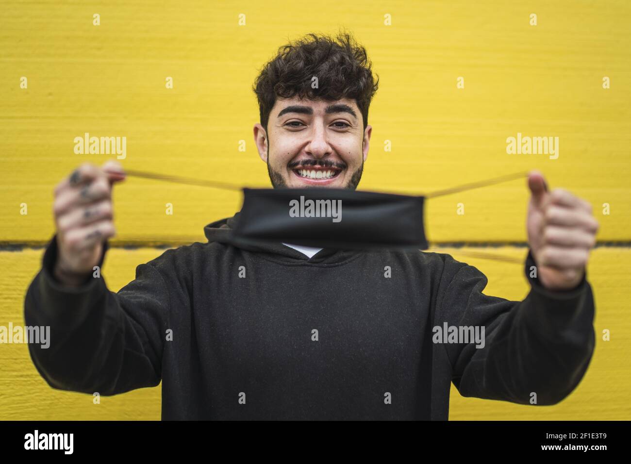 A happy European male showing a face mask on vibrant yellow wall ...