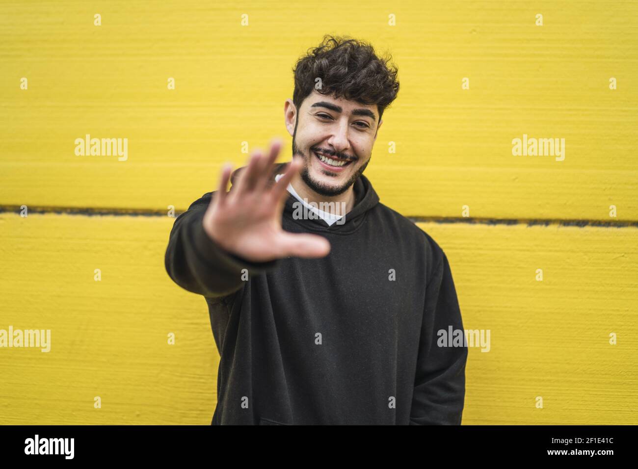 A happy European male showing his hand palm on vibrant yellow wall ...
