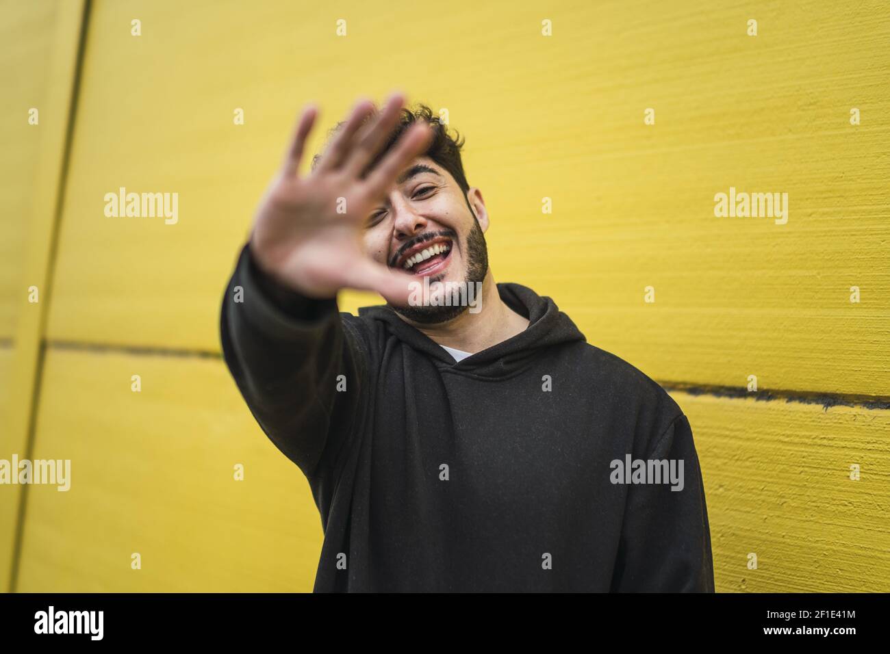 A happy European male showing his hand palm on vibrant yellow wall ...