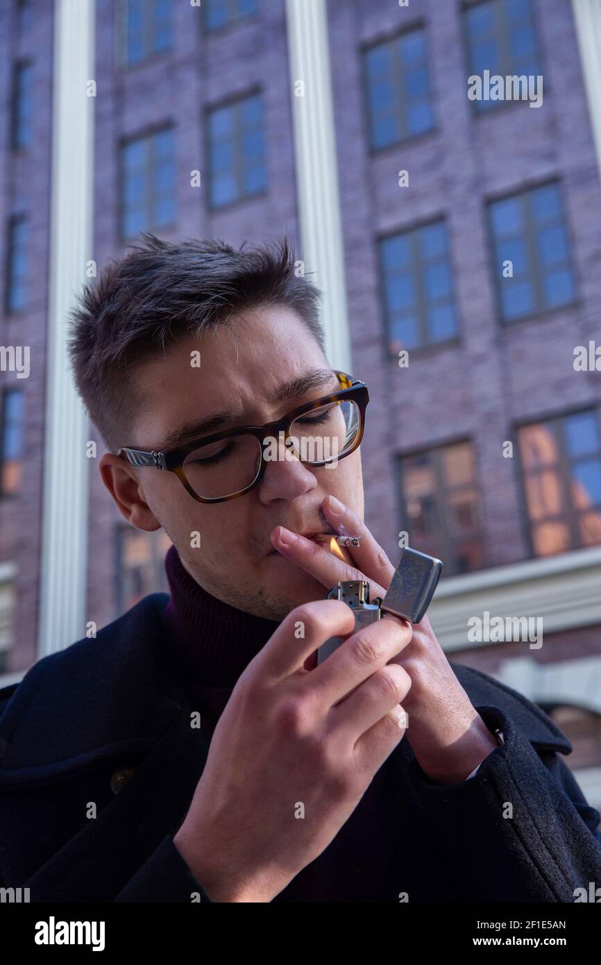 Smoking white european young man with city building behind with a ...
