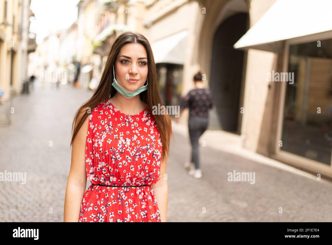Masked young woman walking in a city with a mask lowered on her chin ...