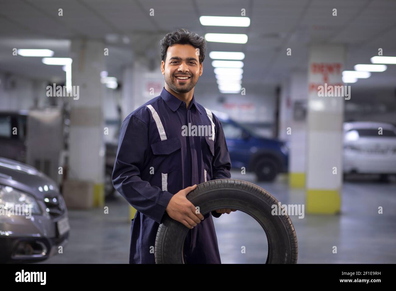 Portrait of smiling mechanic holding a tyre in auto repair shop Stock ...