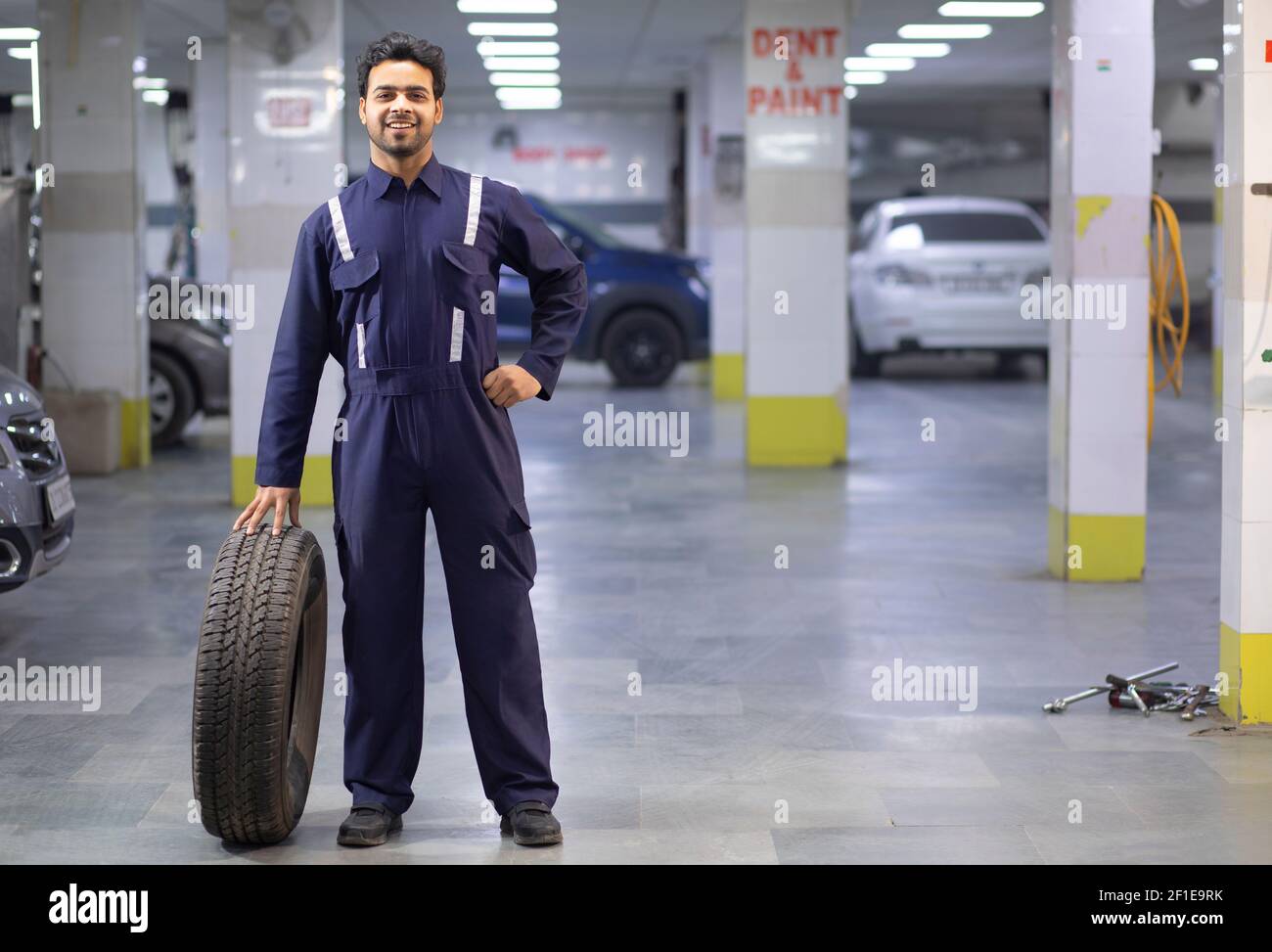 Portrait of smiling mechanic holding a tyre in auto repair shop Stock ...