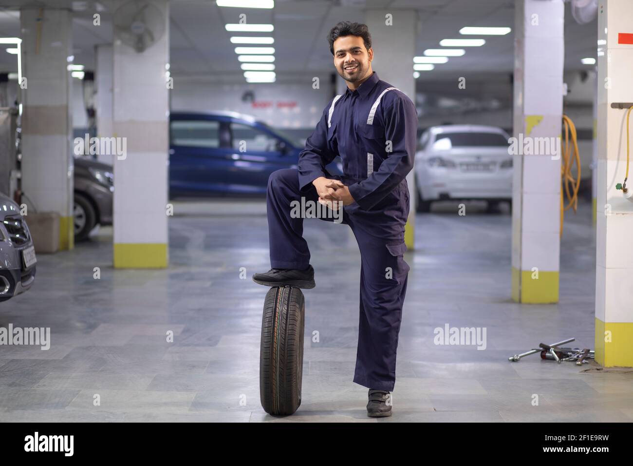 Portrait of smiling mechanic with a foot on a tyre in auto repair shop ...