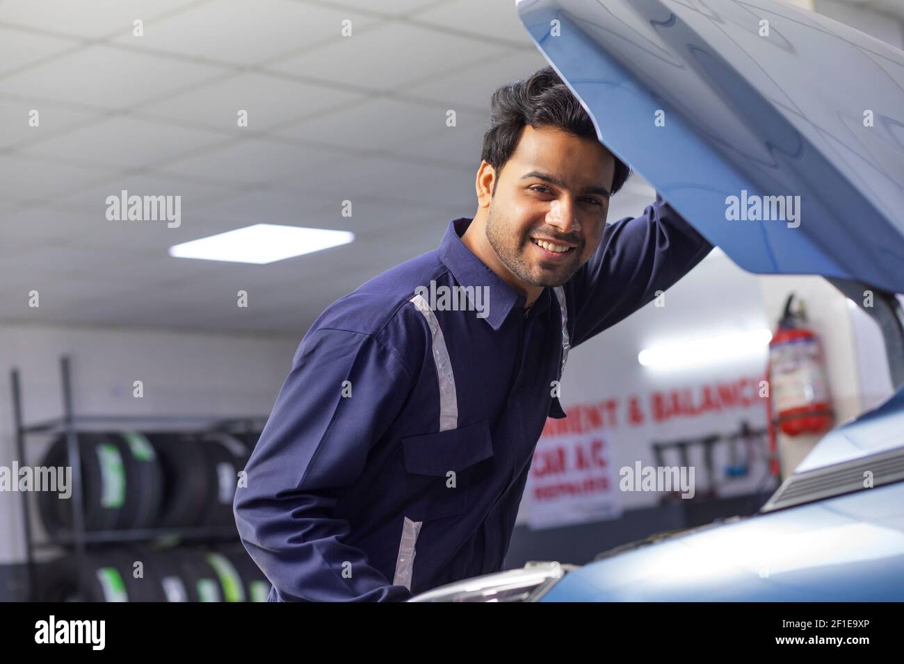 Smiling car mechanic with an open bonnet of a car Stock Photo - Alamy
