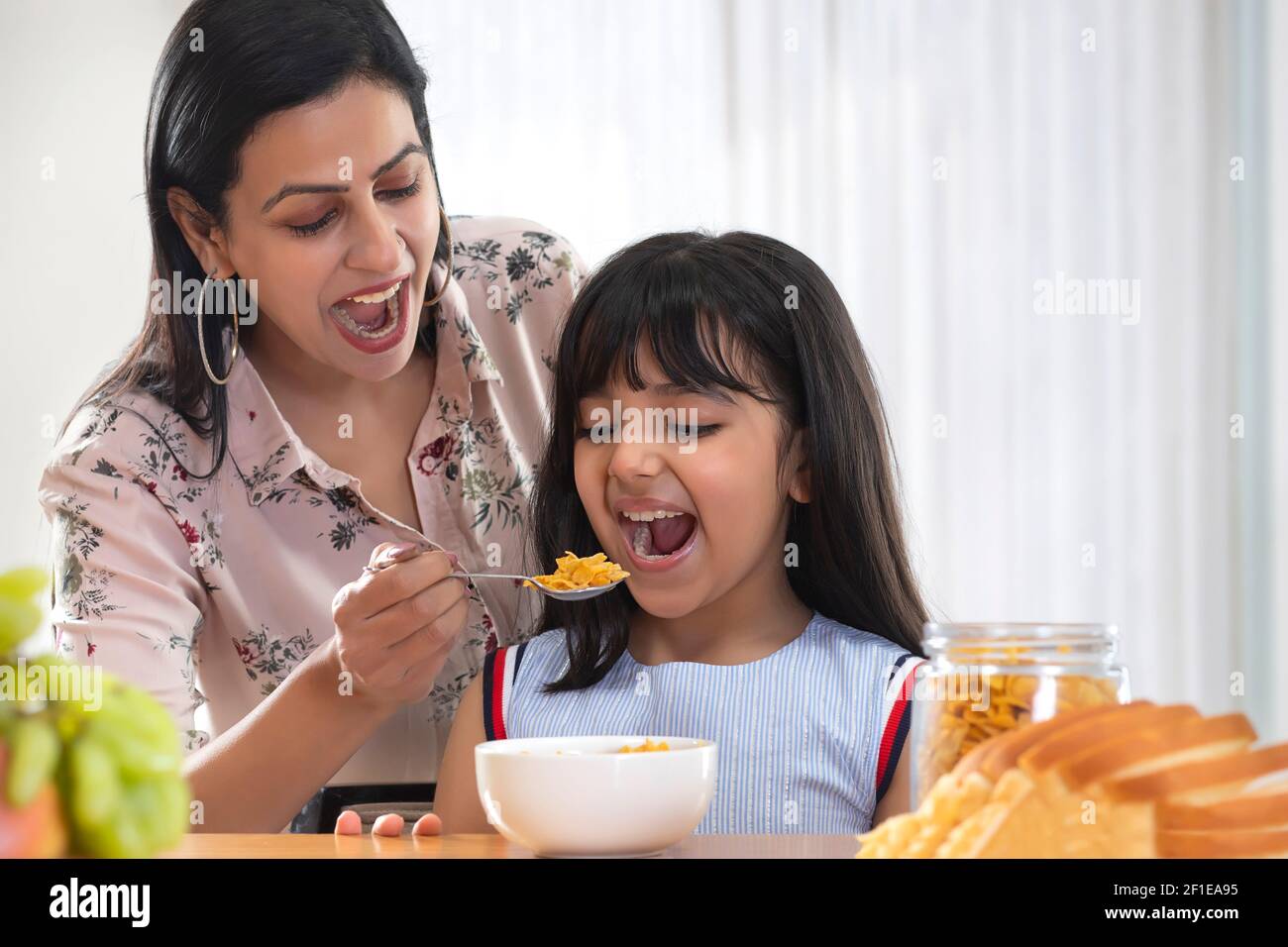 A HAPPY DAUGHTER CHEERFULLY EATING CORNFLAKES GIVEN BY MOTHER Stock ...