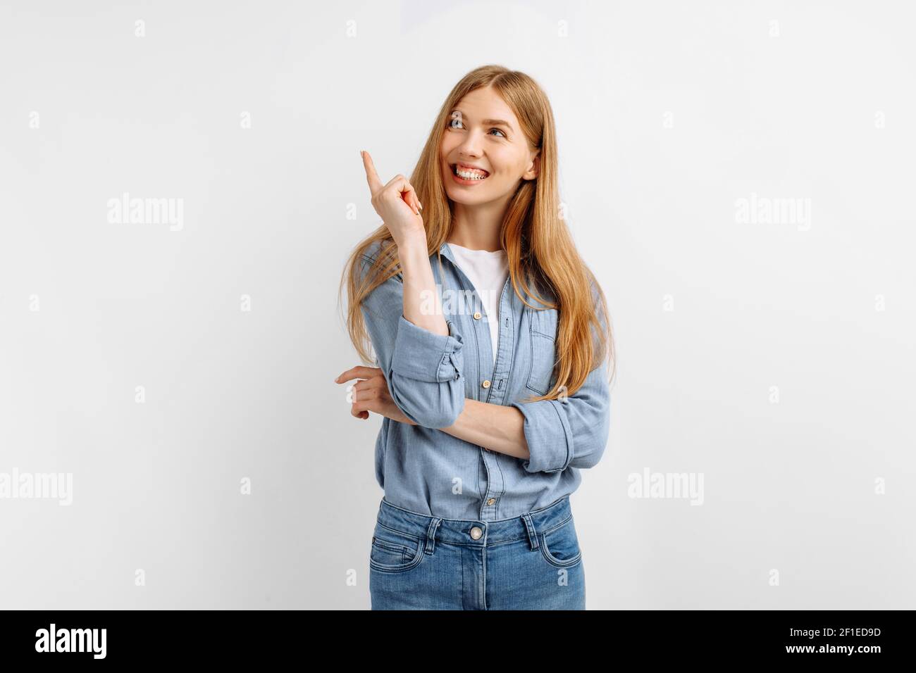 Excited happy young woman points finger up in copy space while standing ...