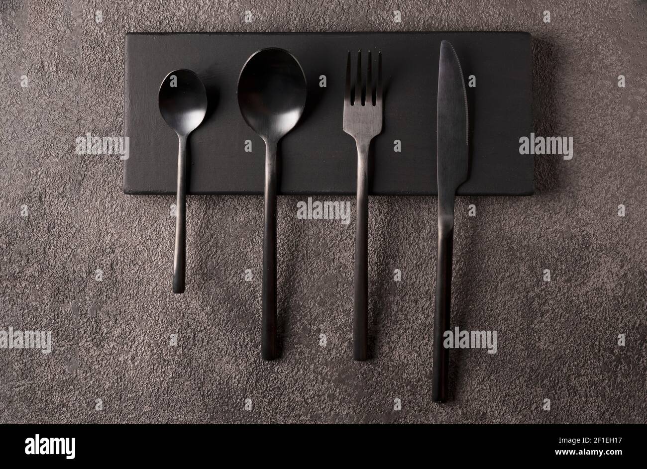 Black cutlery set - fork, spoon, knife, on dark wood . Minimalistic ...