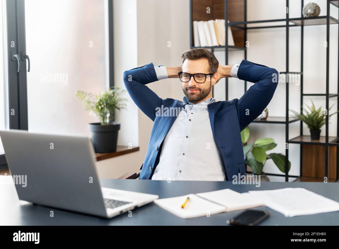 Successful bearded young businessman in business wear, glasses sitting ...
