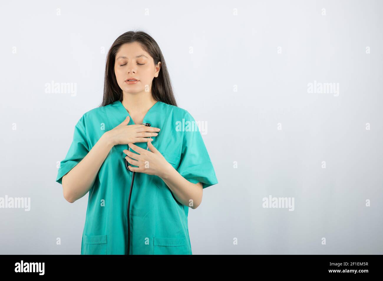 Portrait of female nurse checking her heart by stethoscope on white ...