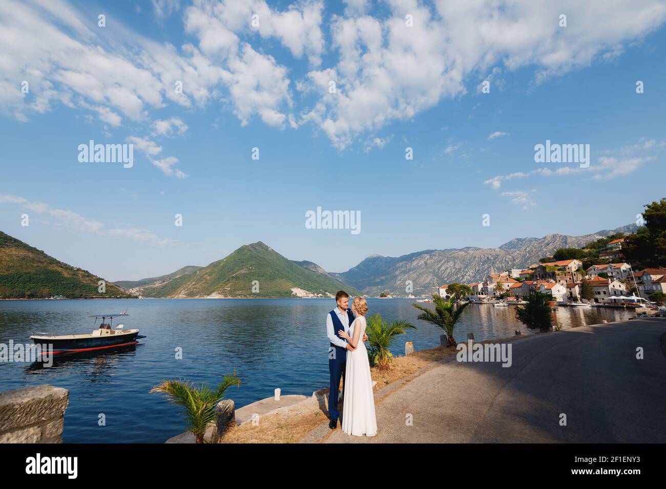 The bride and groom are embracing on the pier in Perast, behind them a ...