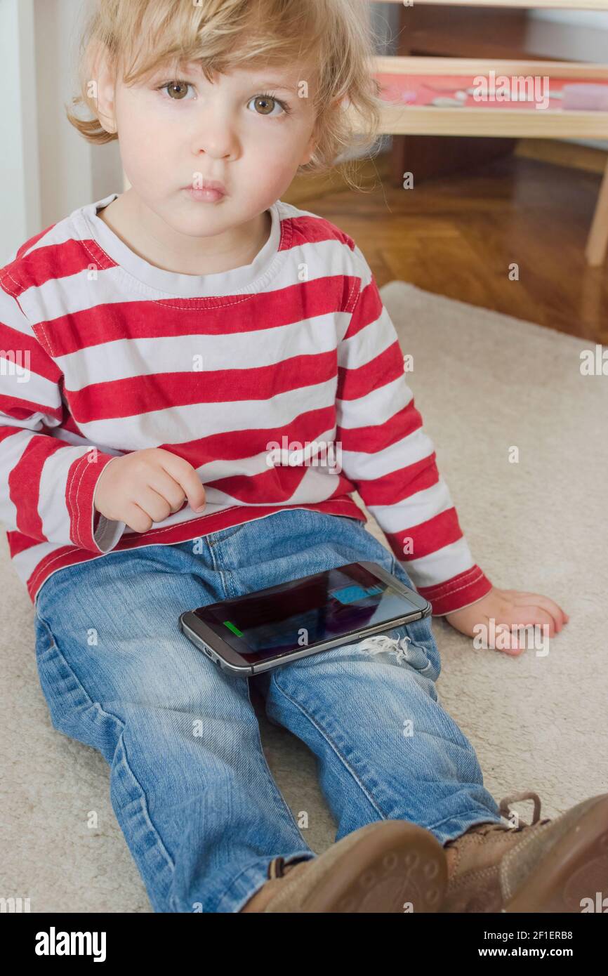 Cute little child using a smartphone while sitting on the floor at home ...