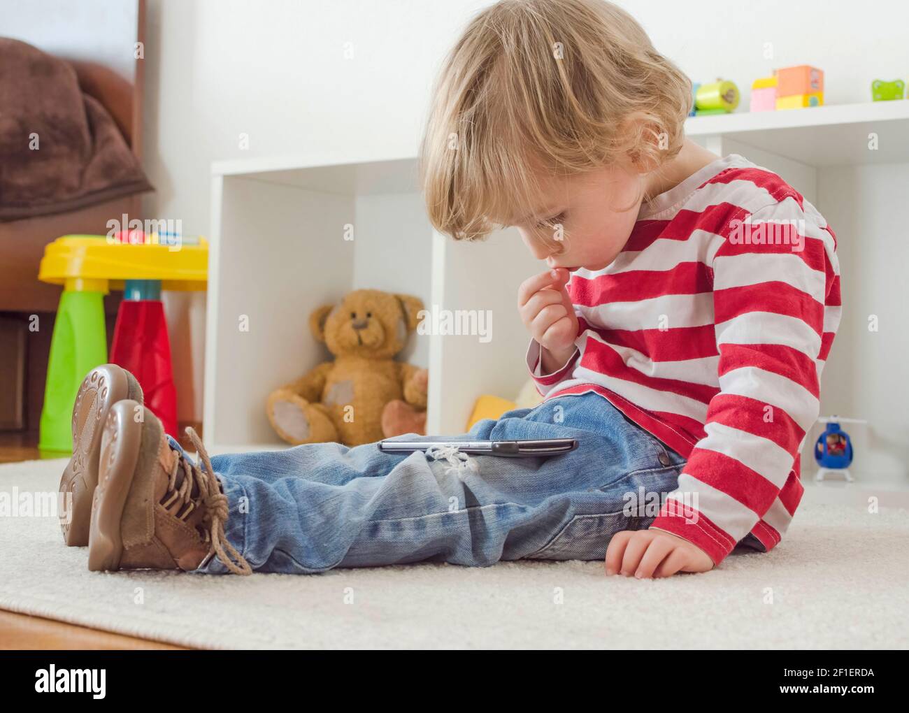 Cute little child using a smartphone while sitting on the floor at home ...