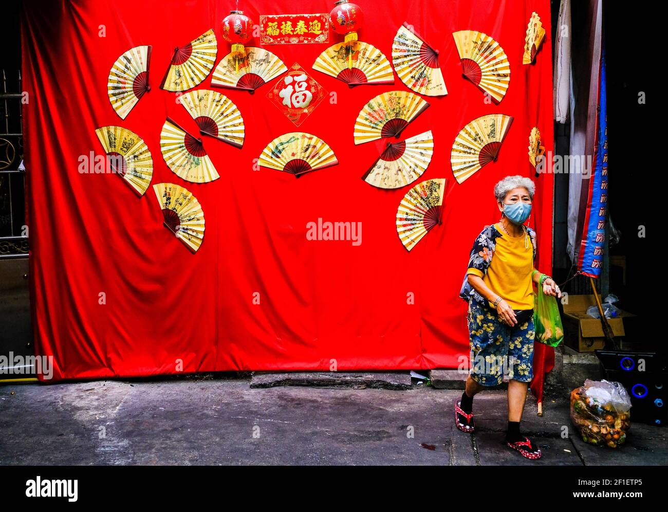 An elderly woman stands in front of a red banner in the Chinatown area ...