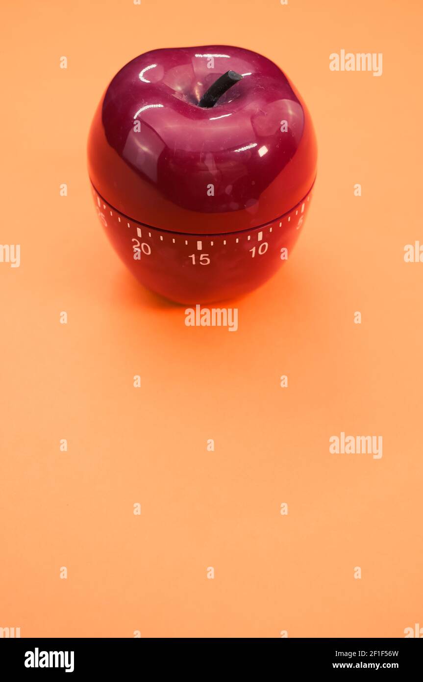 A vertical shot of an apple-shaped kitchen timer isolated on orange ...