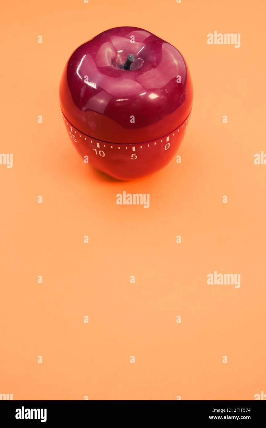A vertical shot of an apple-shaped kitchen timer isolated on orange ...