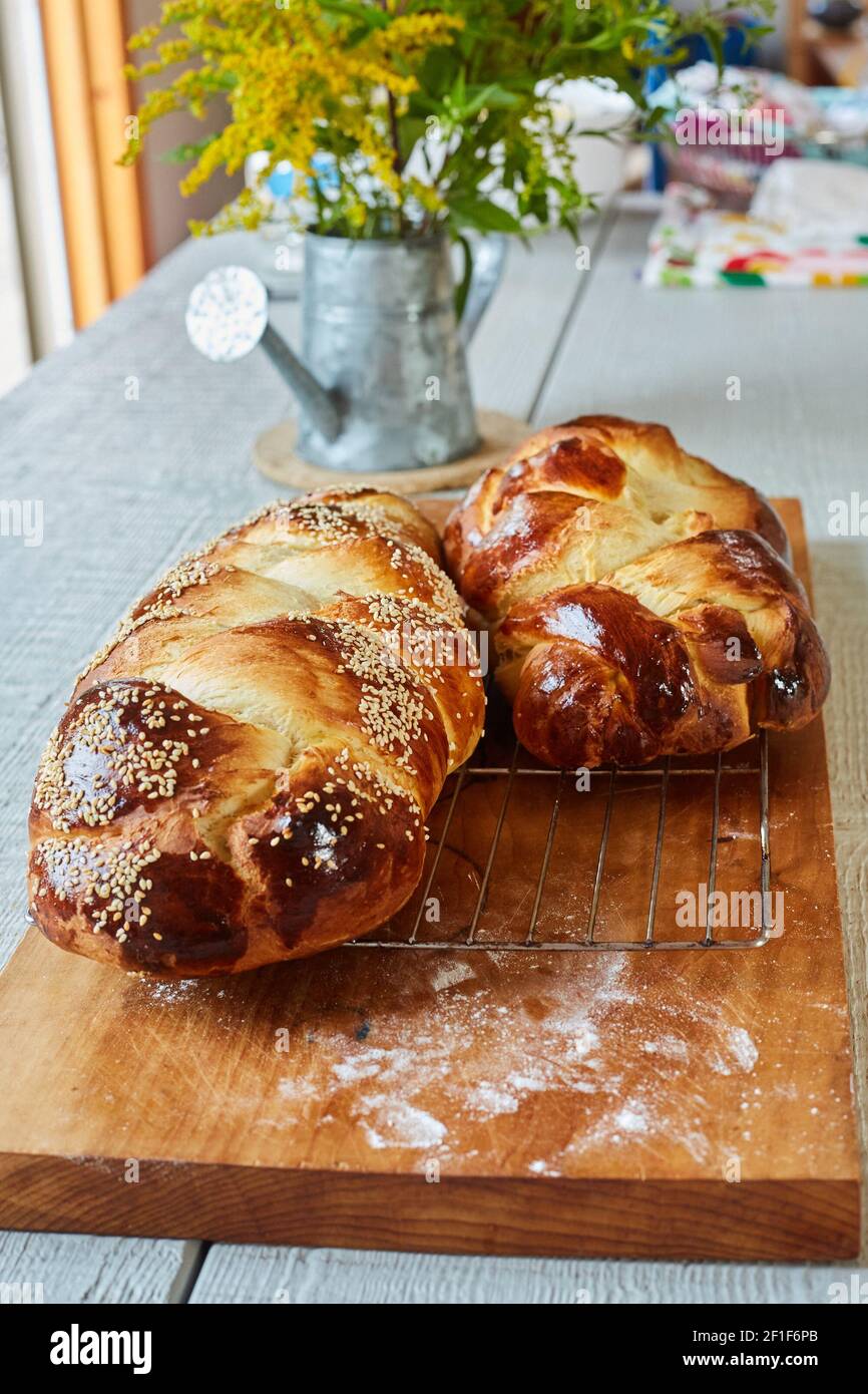 Two Challah Loaves on a Rack Set on a Cutting Board with Wildflowers in ...
