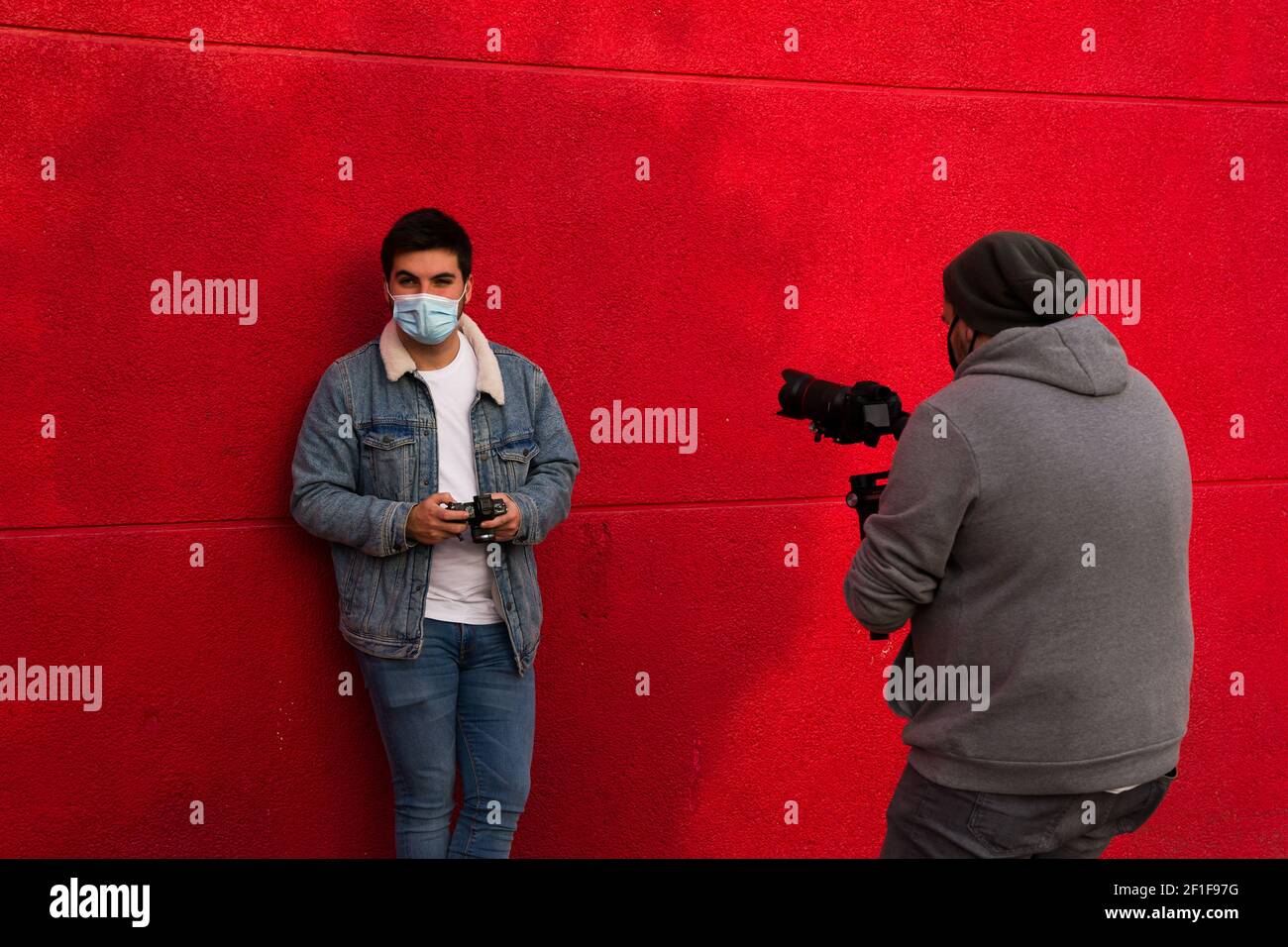 A side view of a cameraman shooting a young handsome guy standing by a ...