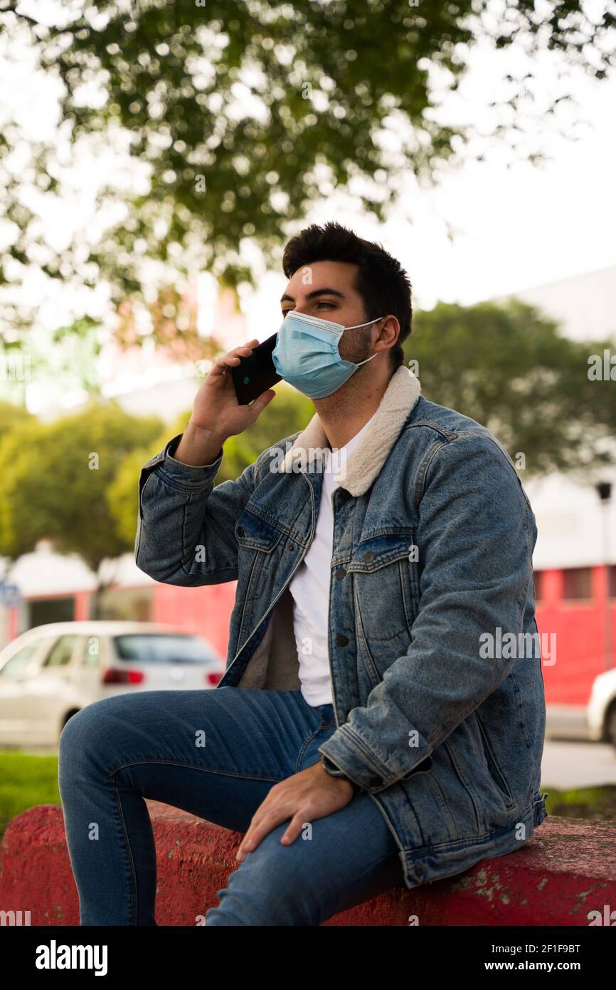 A side view of a young handsome man with a medical face mask talking on ...