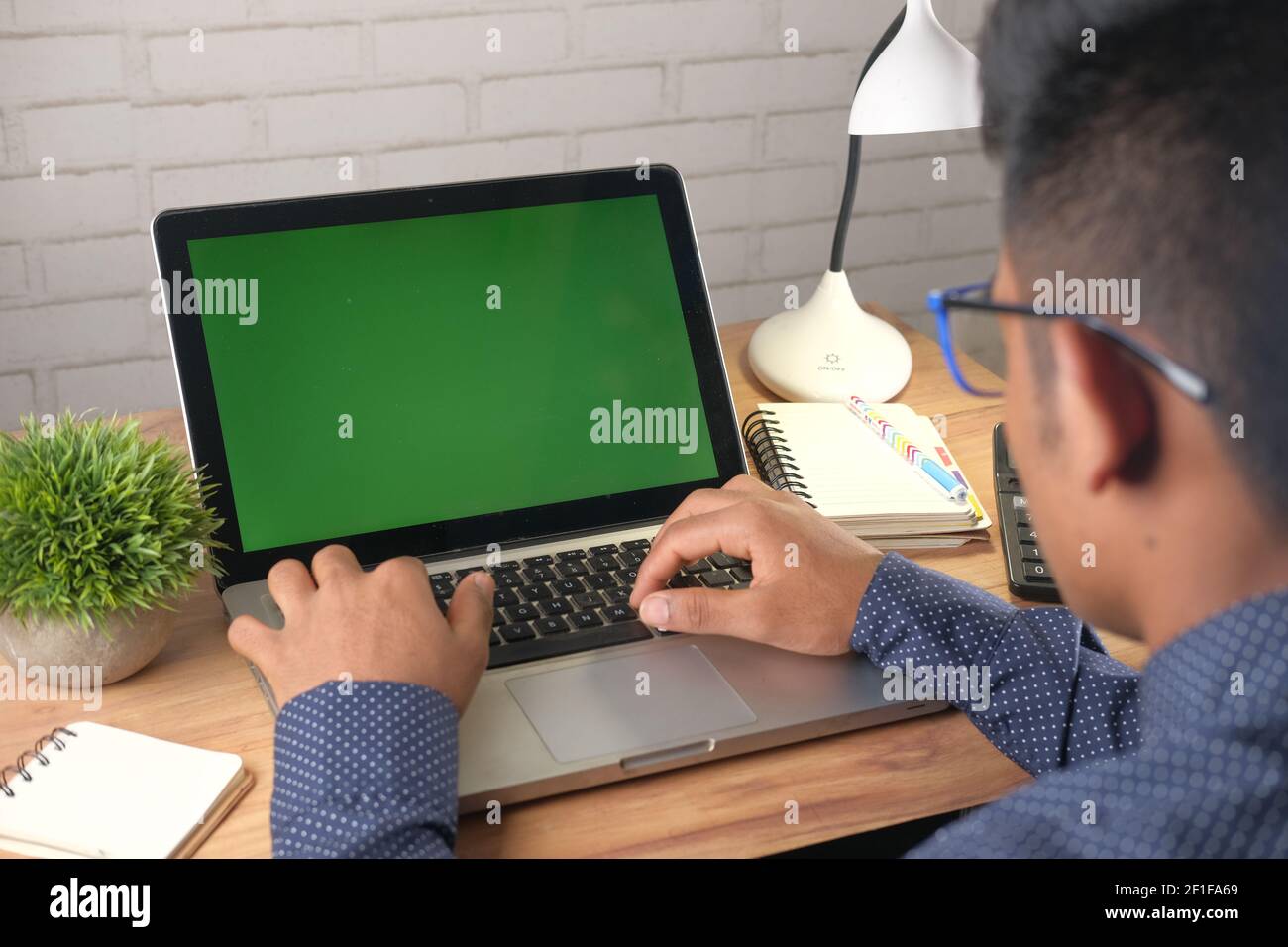 rear view of young man using laptop with blank screen on office desk ...