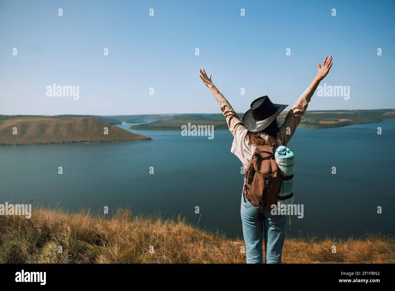 Young female tourist in cowboy hat holding hands up while standing on ...