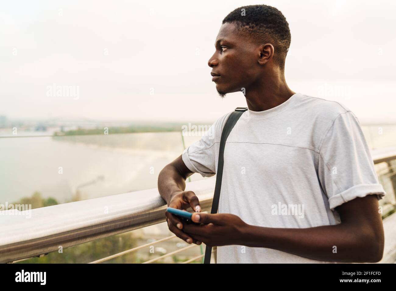 Serious african american guy using mobile phone on urban bridge ...