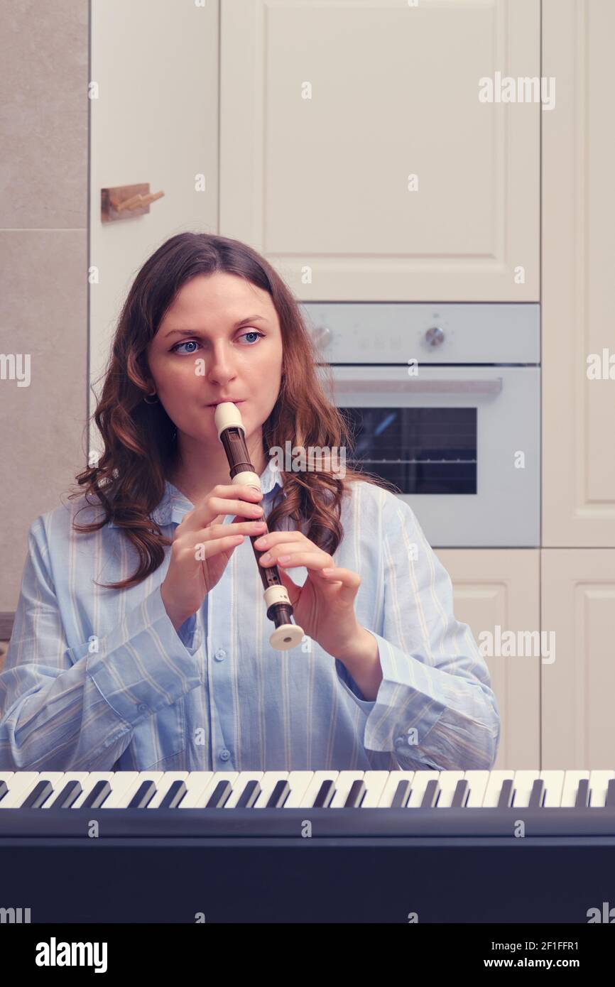 Woman playing the block flute while sitting in the home kitchen by the ...