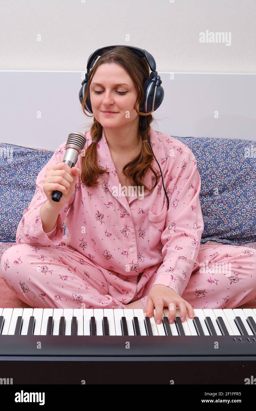 A female musician sings into a microphone and plays the piano on a home ...