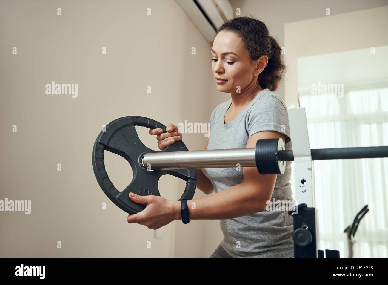 A young fit woman putting a metal disc on a barbell during heavy ...