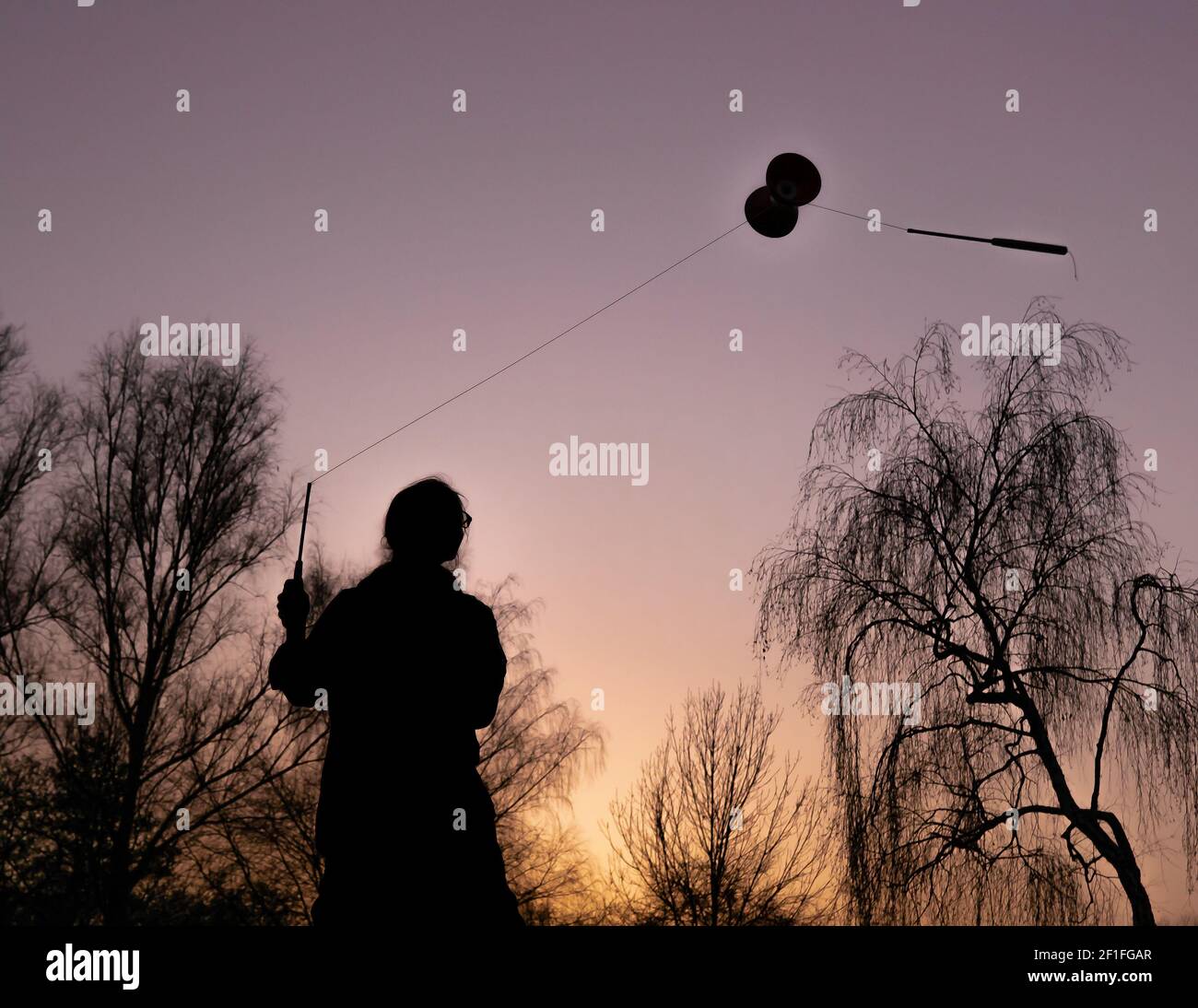 Silhouette of a girl playing with diabolo at sunset in a spring park ...