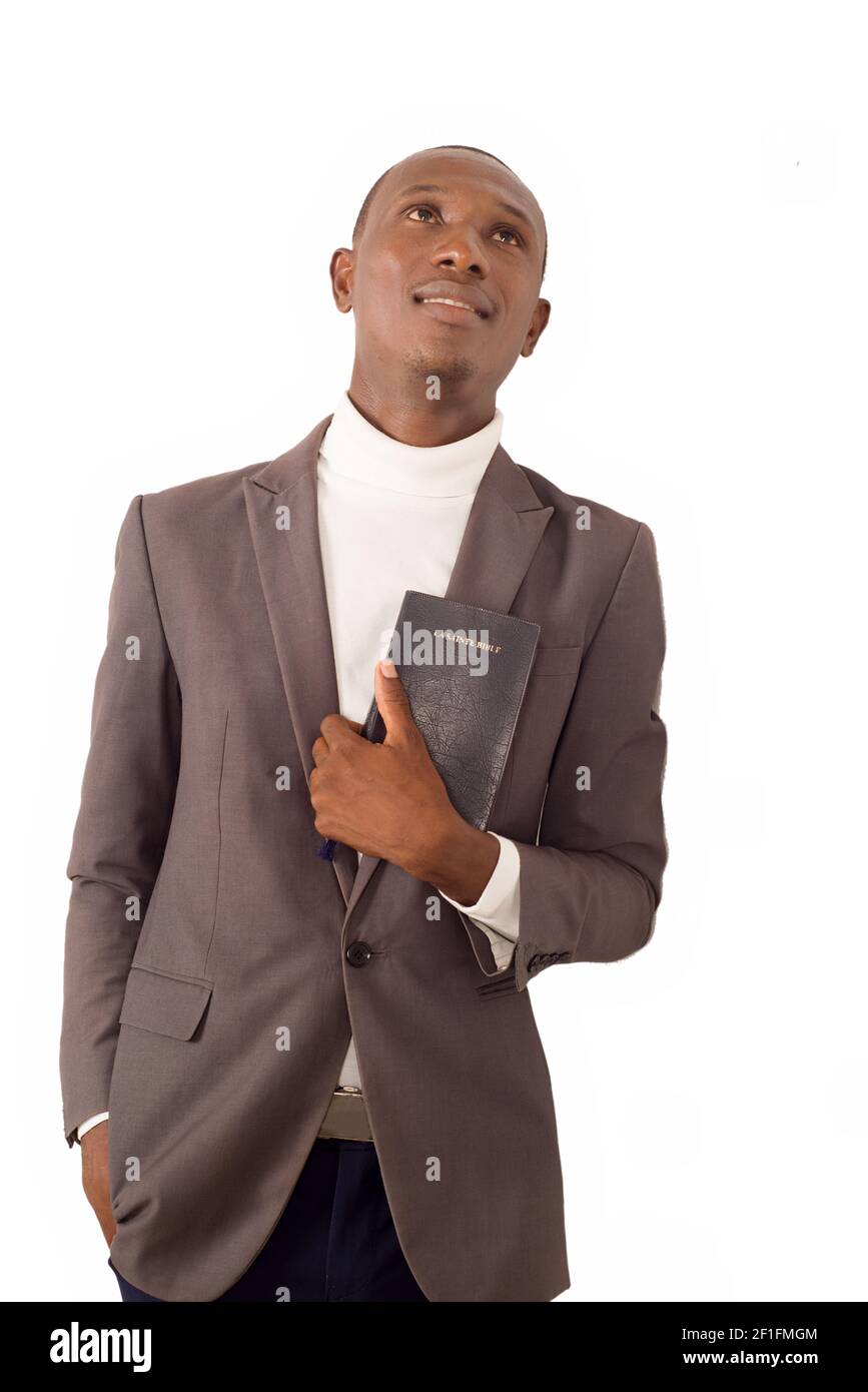 young smiling pastor standing in jacket and holding a Bible on white ...