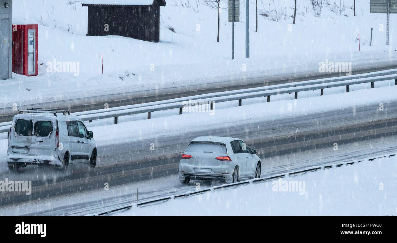 Cars driving on a highway in a blizzard with the road covered in snow ...