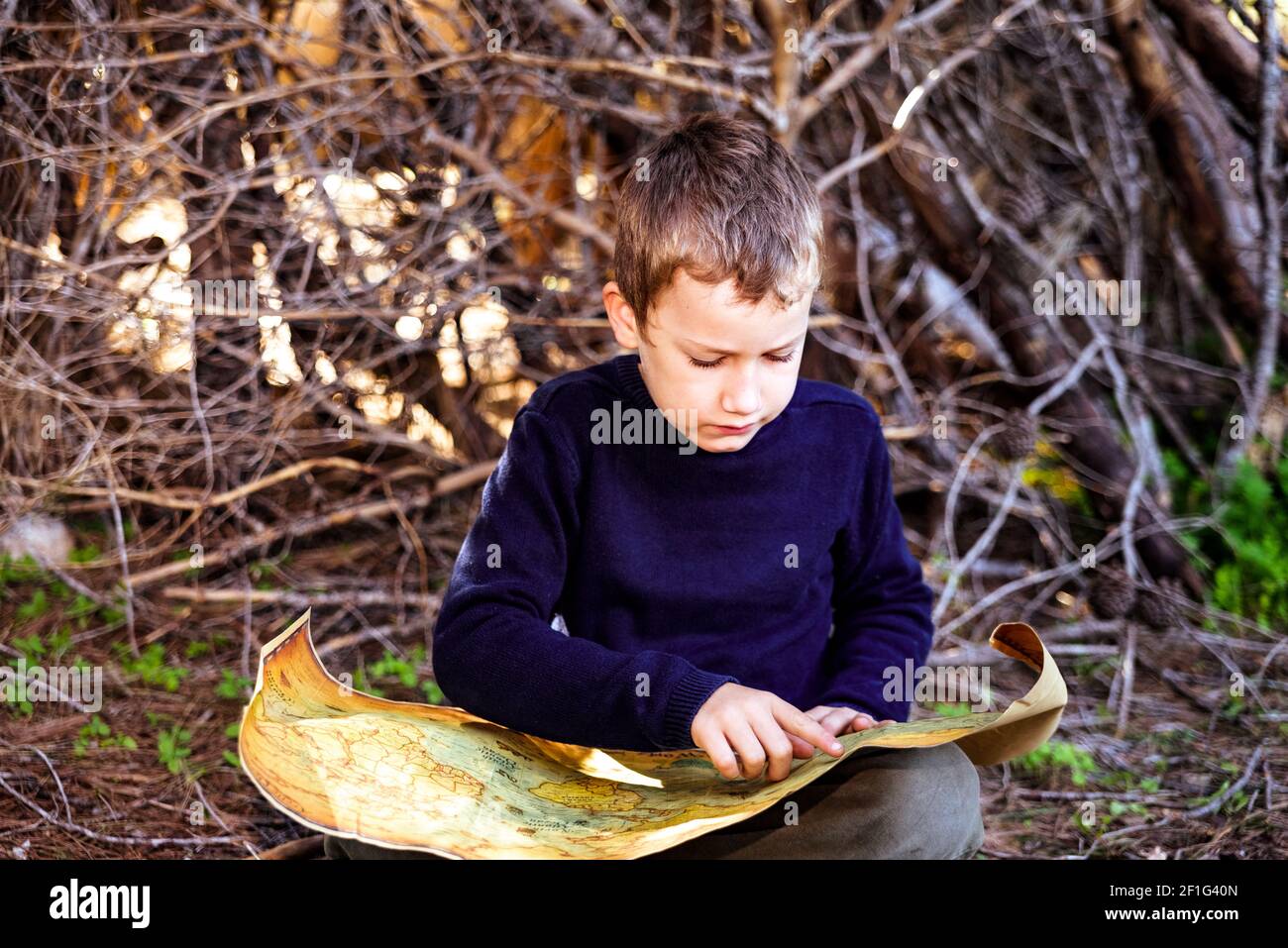 Boy trying to read an old travel map, lost in a forest, in search of ...