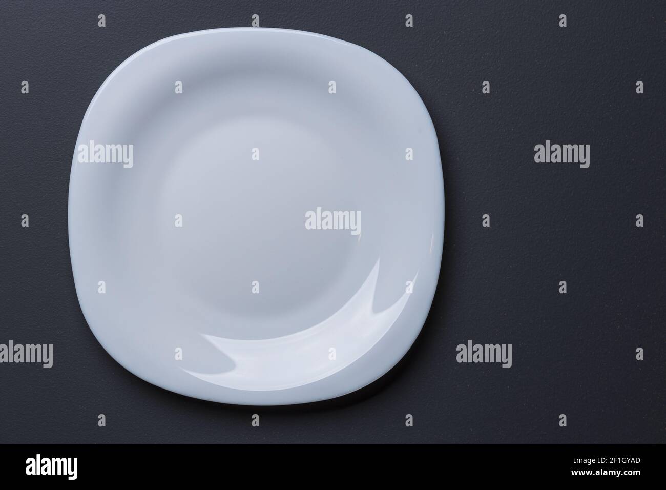 Close up view of white square shaped plate on black background. Black ...