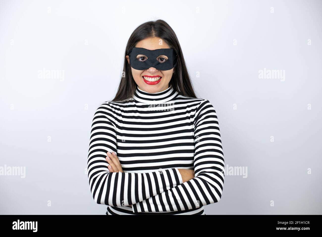 Young beautiful brunette burglar woman wearing mask with a happy face ...