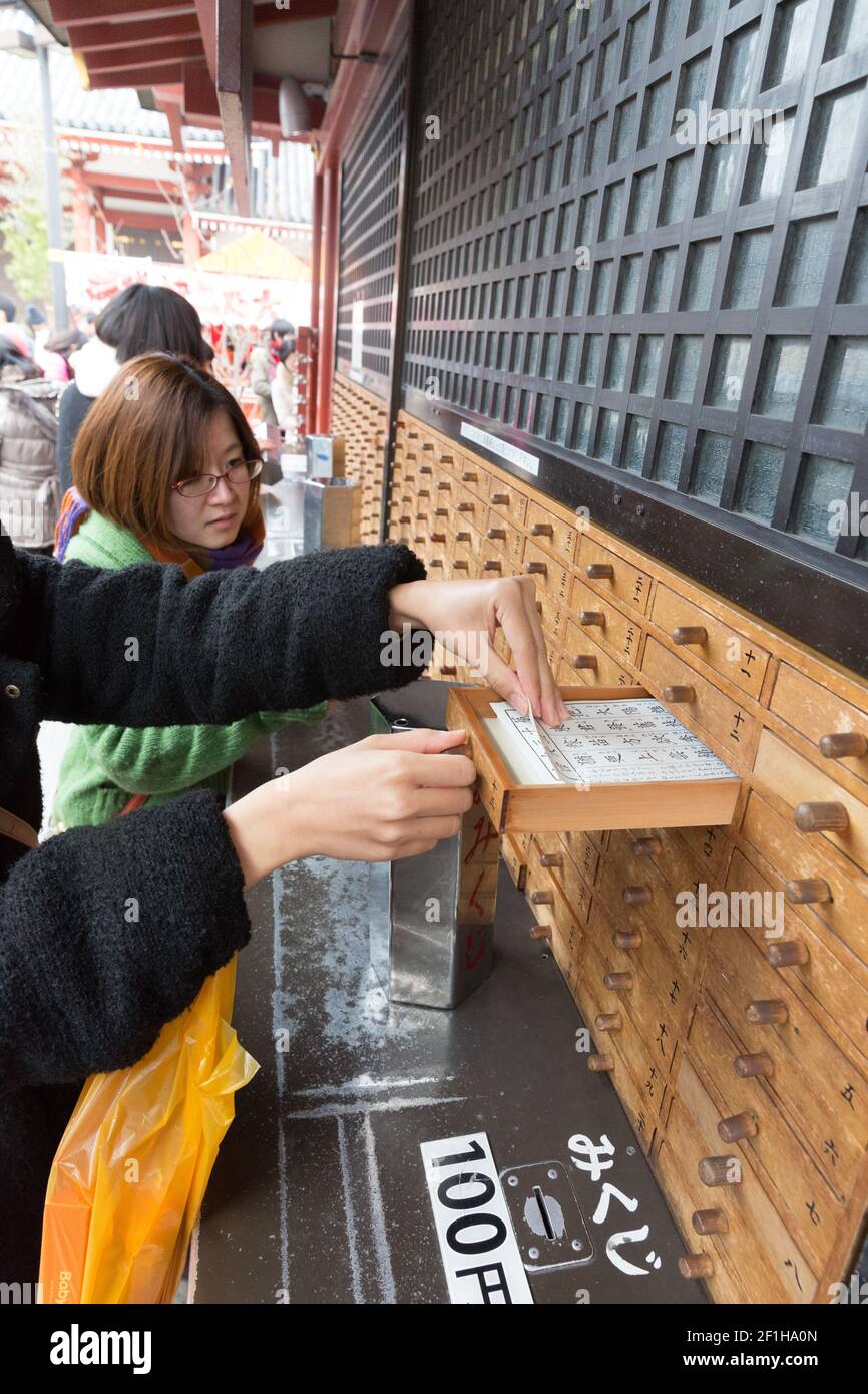 Young Women drawing an Omikuji stick as part of Omikuji fortune telling at Sensoji Temple bring ...