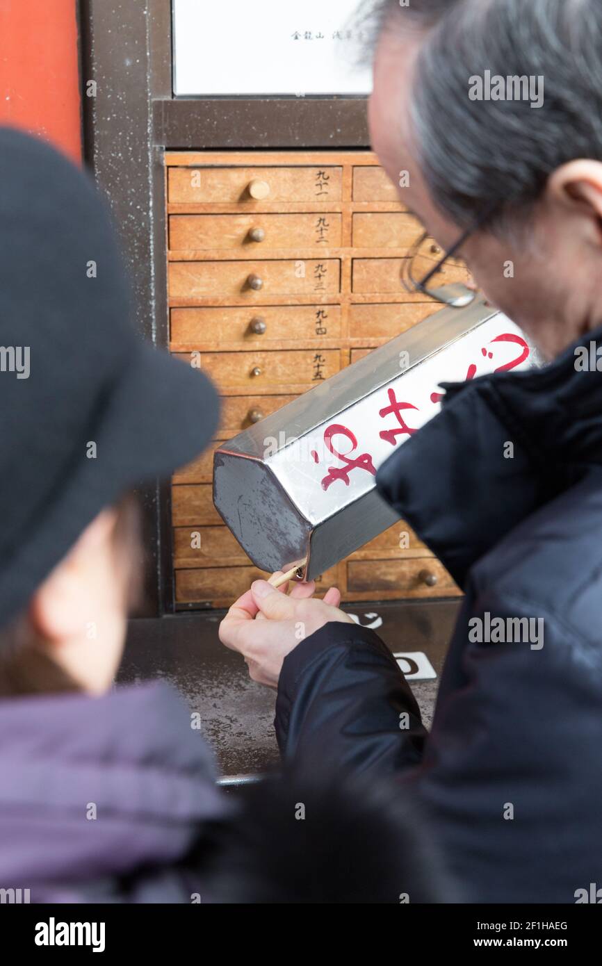 Man collecting his paper strip fortune as a as part of Omikuji fortune telling at Sensoji Temple ...