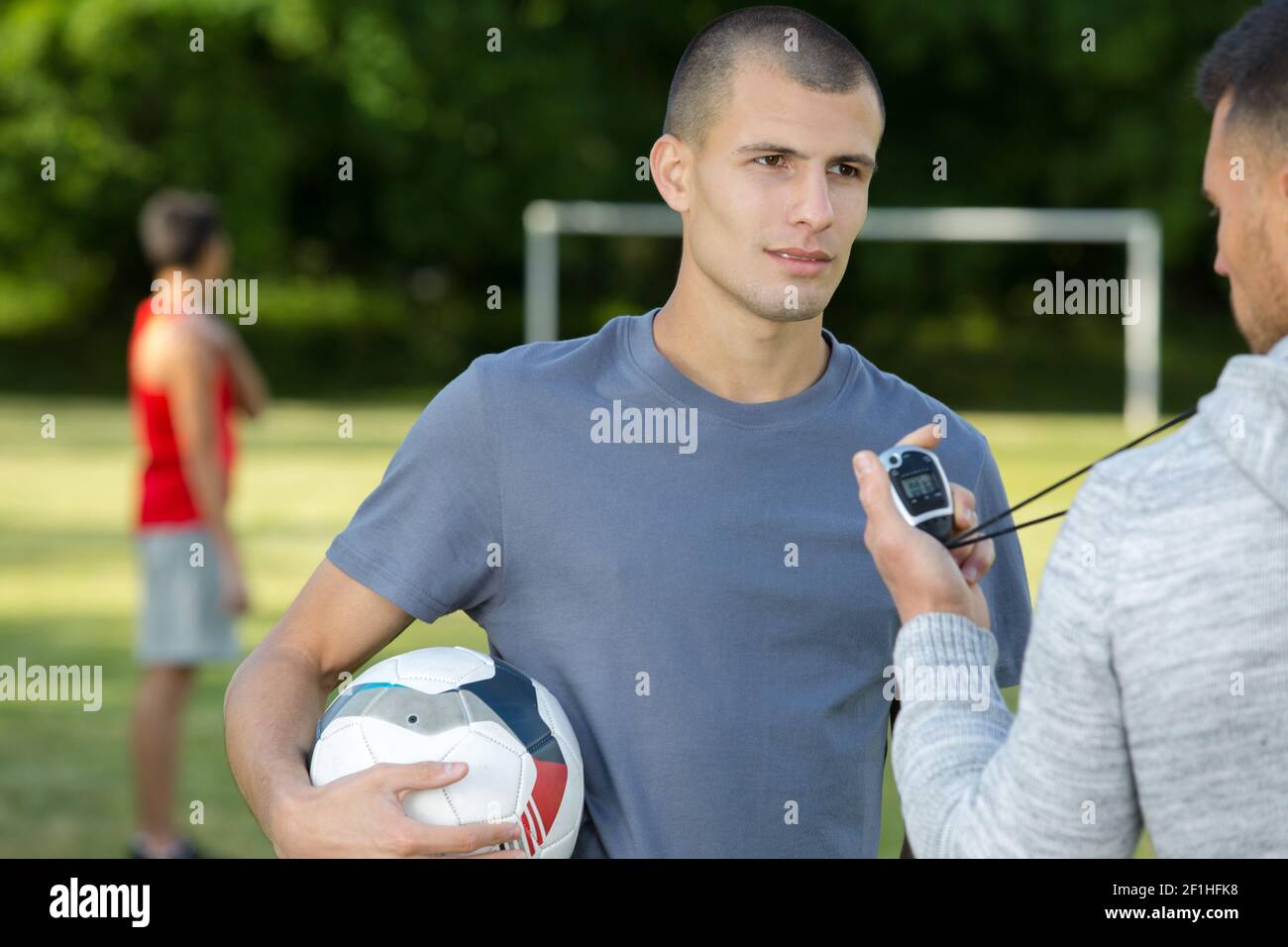 football coach holding a stopwatch and talking to young footballer ...