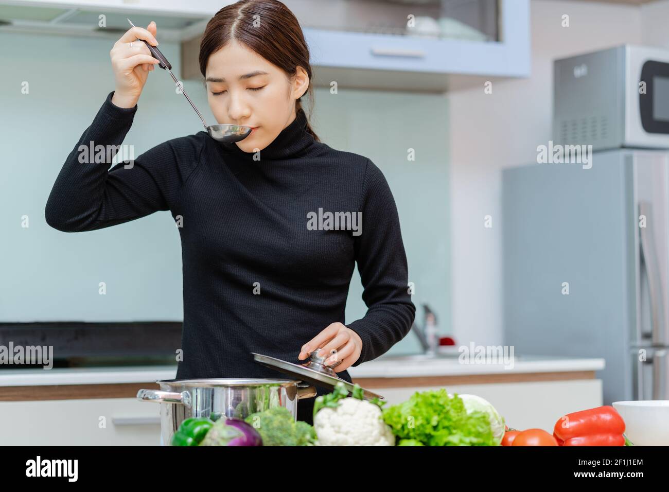 the woman is tasting the soup she cooks Stock Photo - Alamy