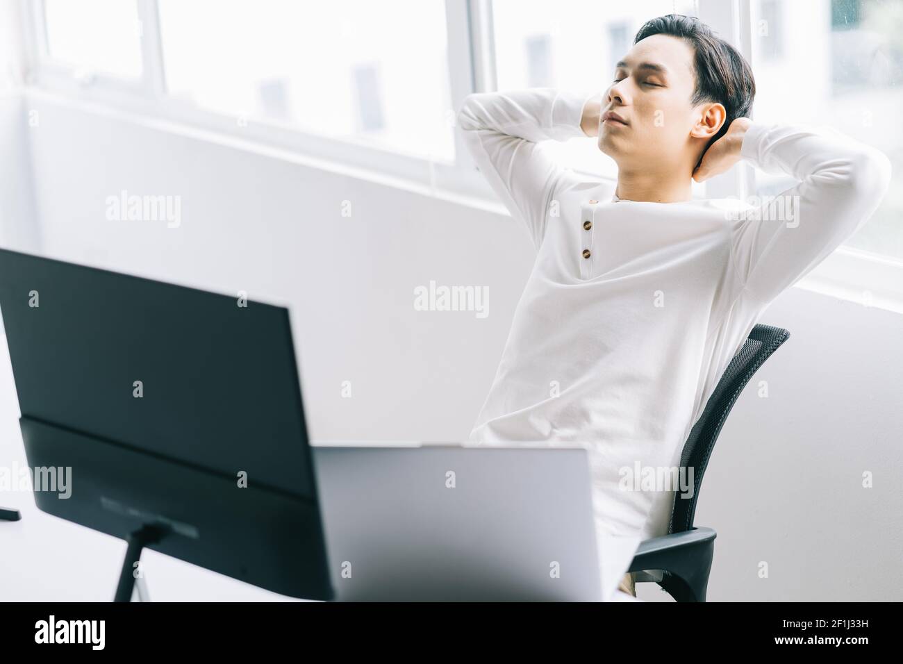 Asian programmer sits with his head back in his chair to relax after a ...