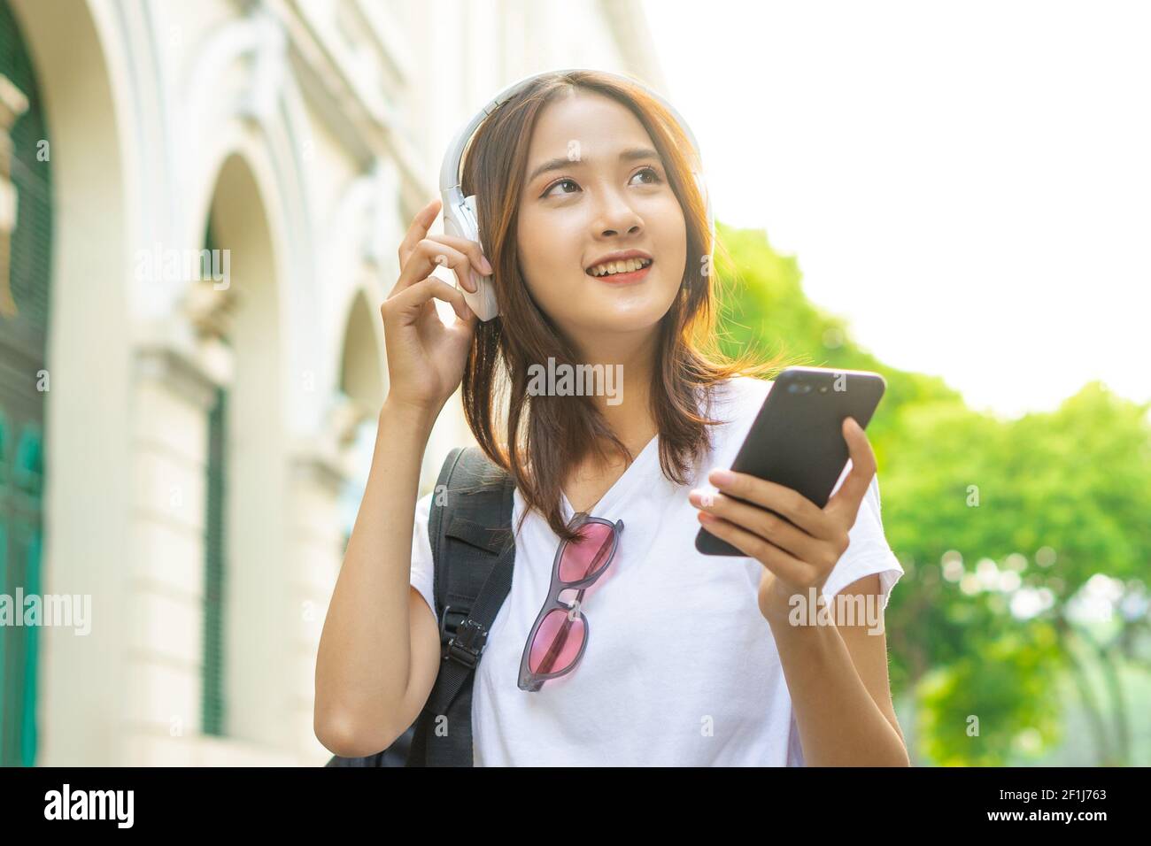 Young Asian girl reading text on her phone and wearing headphones to ...