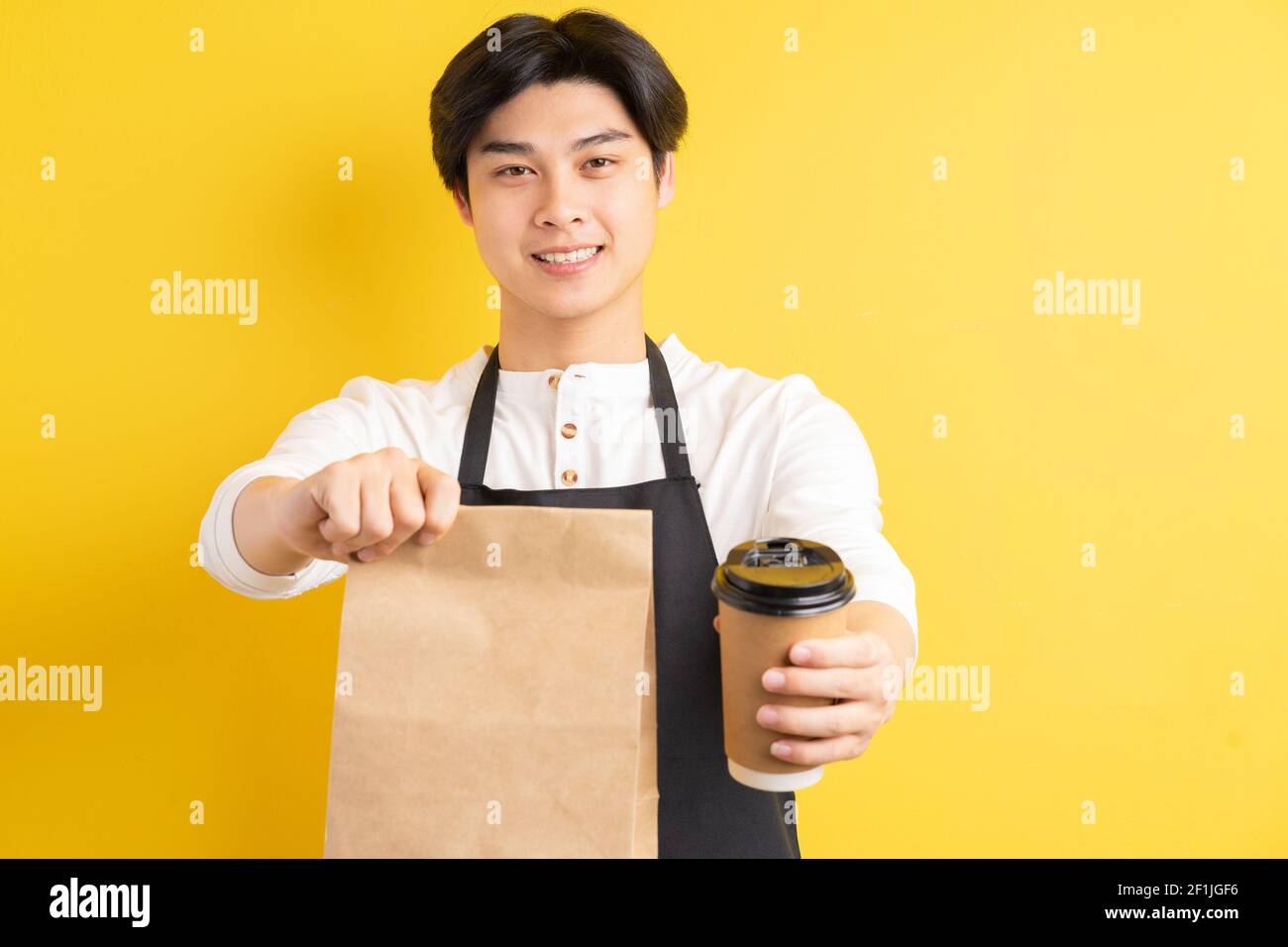 Portrait of male waiter holding paper cup in hand on yellow background ...