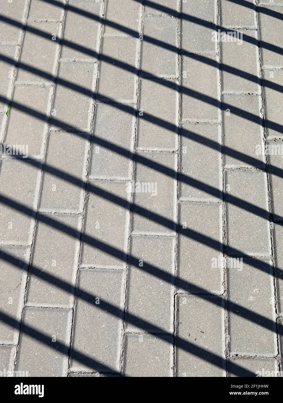 Railing uprights casting shadow on white block paving Stock Photo - Alamy