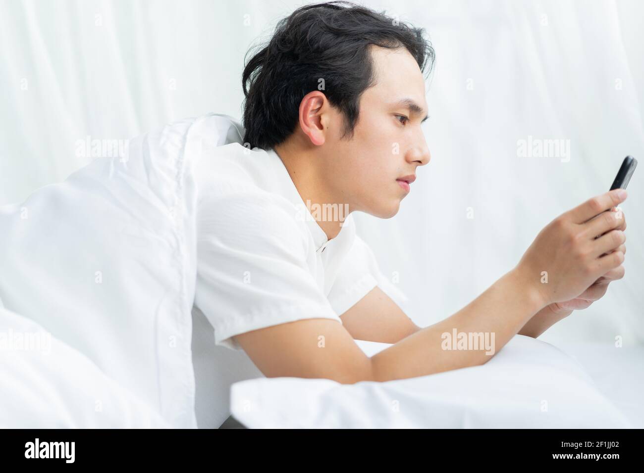 Young man lying in bed using a phone Stock Photo - Alamy