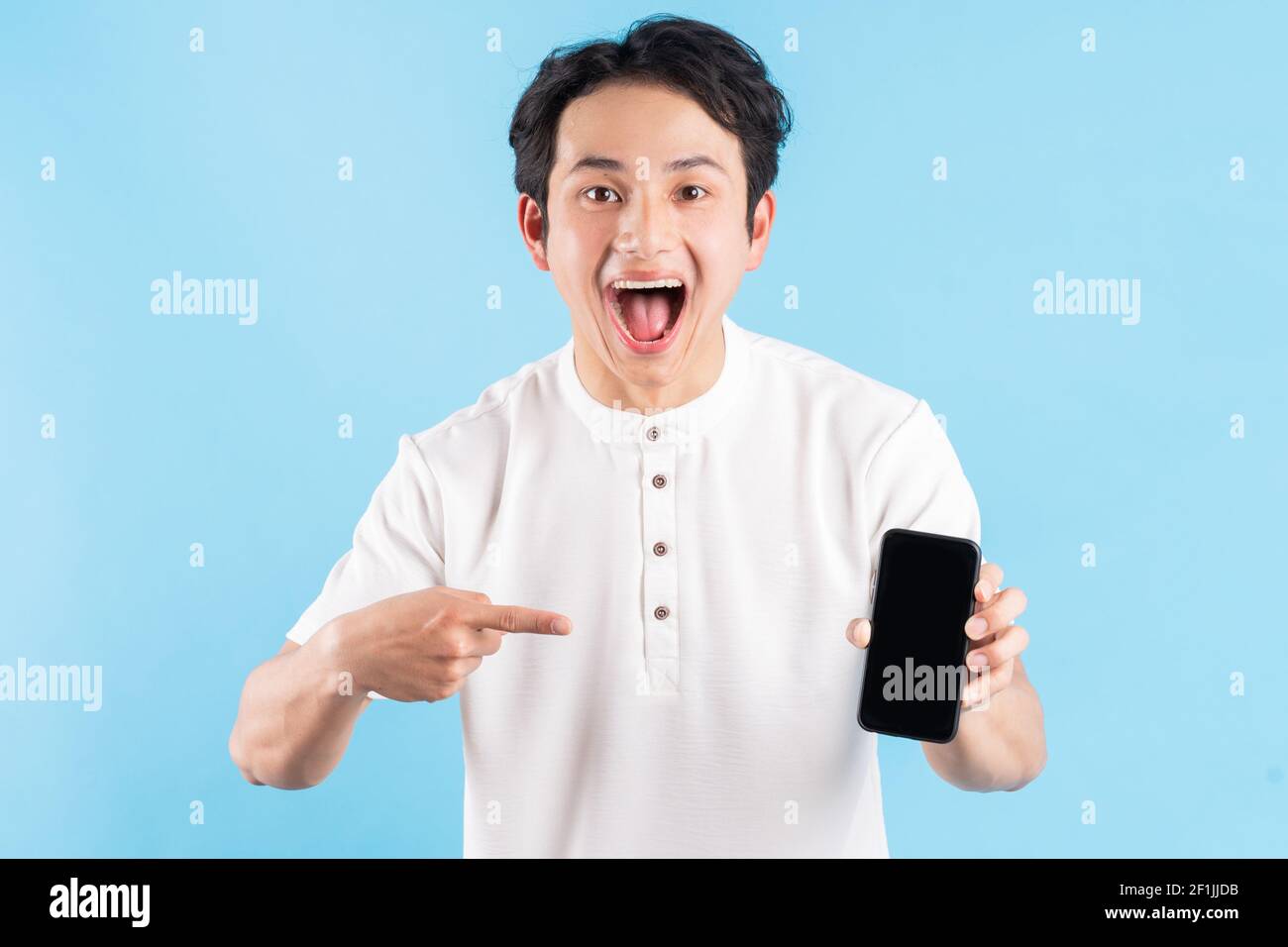 Young smiling man holding a modern smartphone in his hand and pointing ...