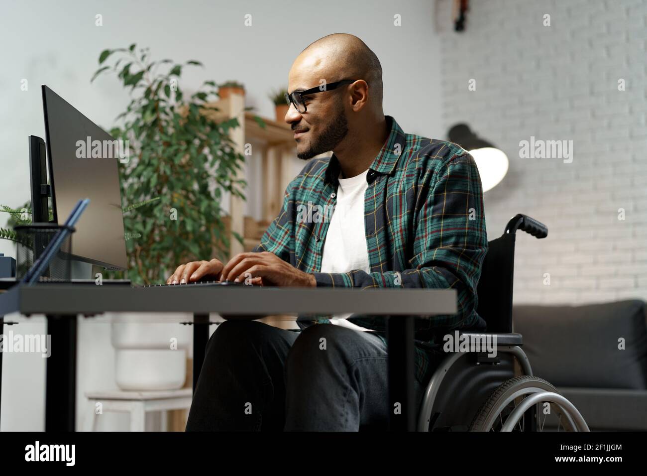 Disabled young african american man in wheelchair using computer while ...