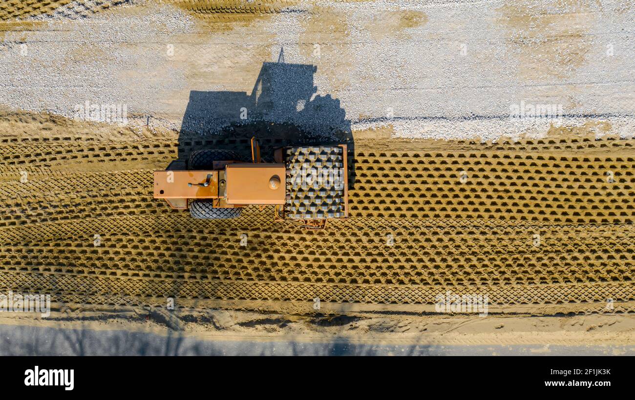 Above top view, overhead on huge road roller with spikes is compacting ...