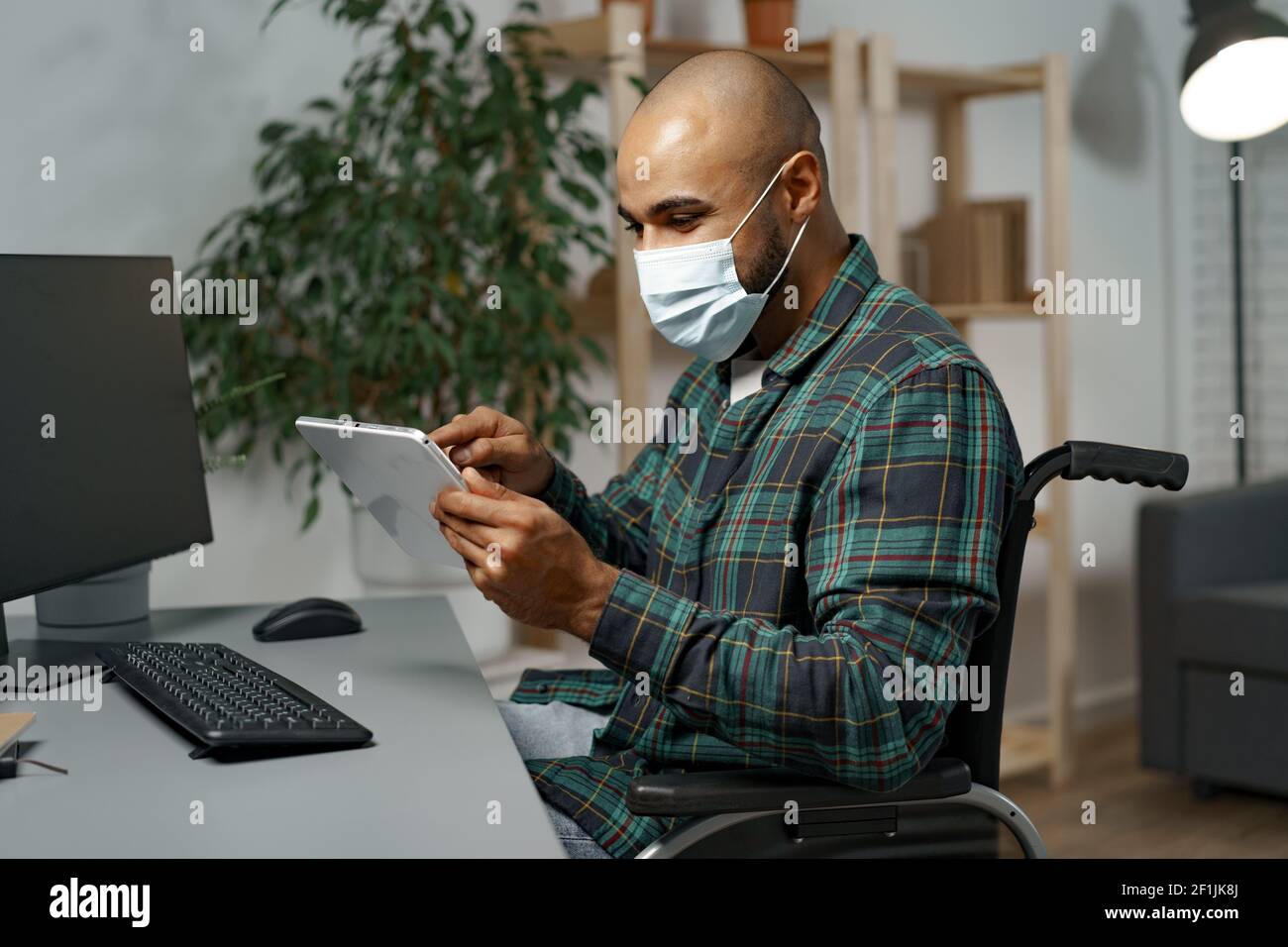 Young disabled man in wheelchair sitting at his working table wearing ...