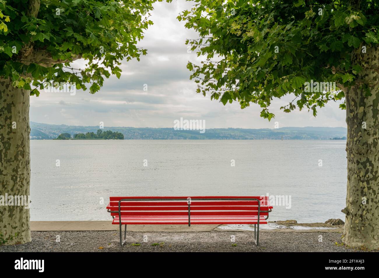Red park bench on a lake shore with a fantastic view and framed by ...